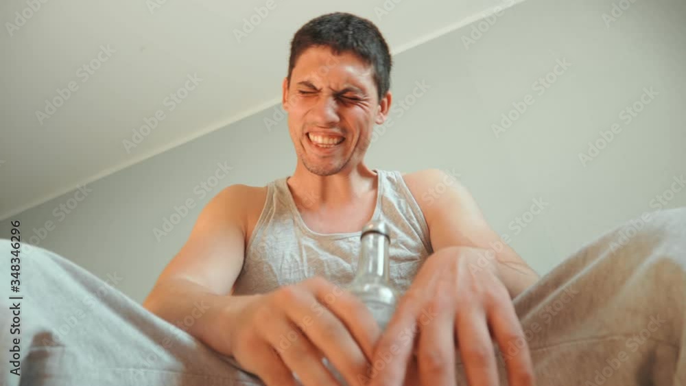 A young guy with bruised eye in an alcoholic intoxication drinks vodka ...