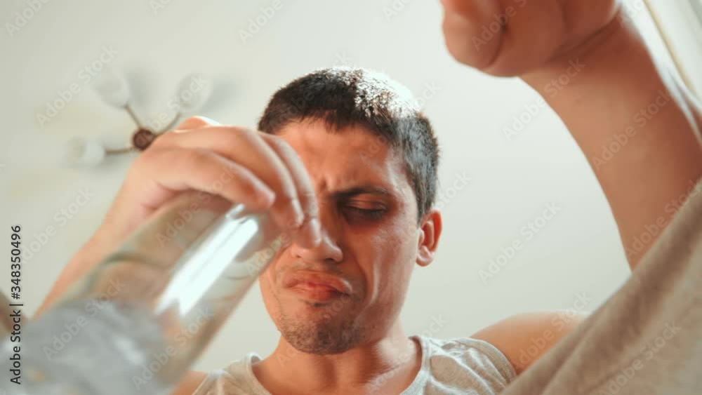 A young guy with bruised eye in an alcoholic intoxication drinks vodka ...