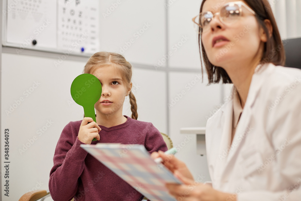 Foto de Portrait of cute little girl reading test chart during vision ...