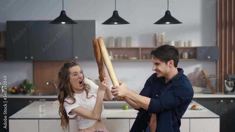 Man and woman fighting with rolling pins on kitchen. Couple having fun ...