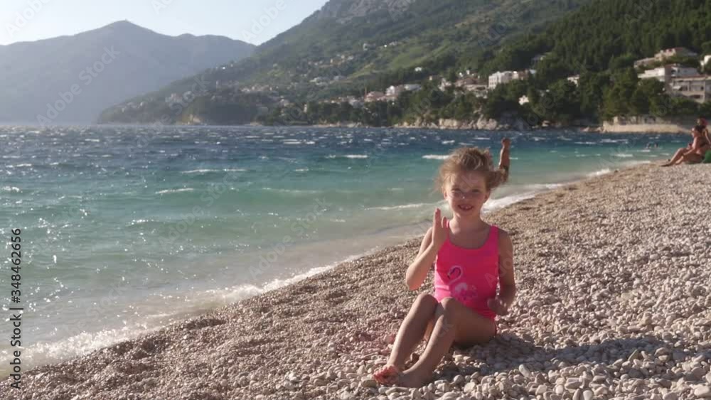 Little girl sits and waving hand on the beach at sunset, Makarska ...
