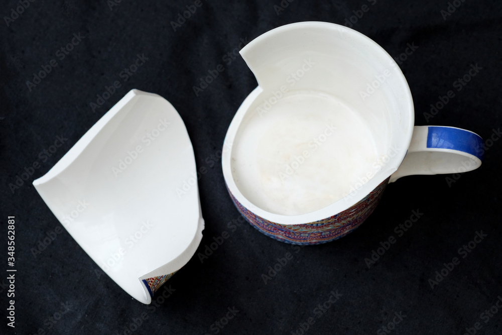 Broken ceramic cup on a black background. Two parts of a white cup with ...