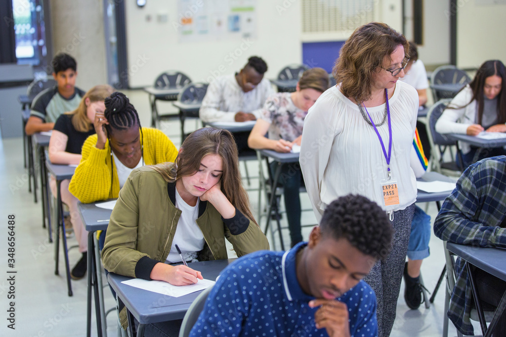 High school teacher supervising students taking exam desks classroom ...