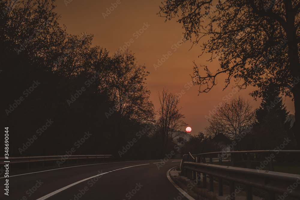 Red crimson sun is setting down behind a country road with visible ...