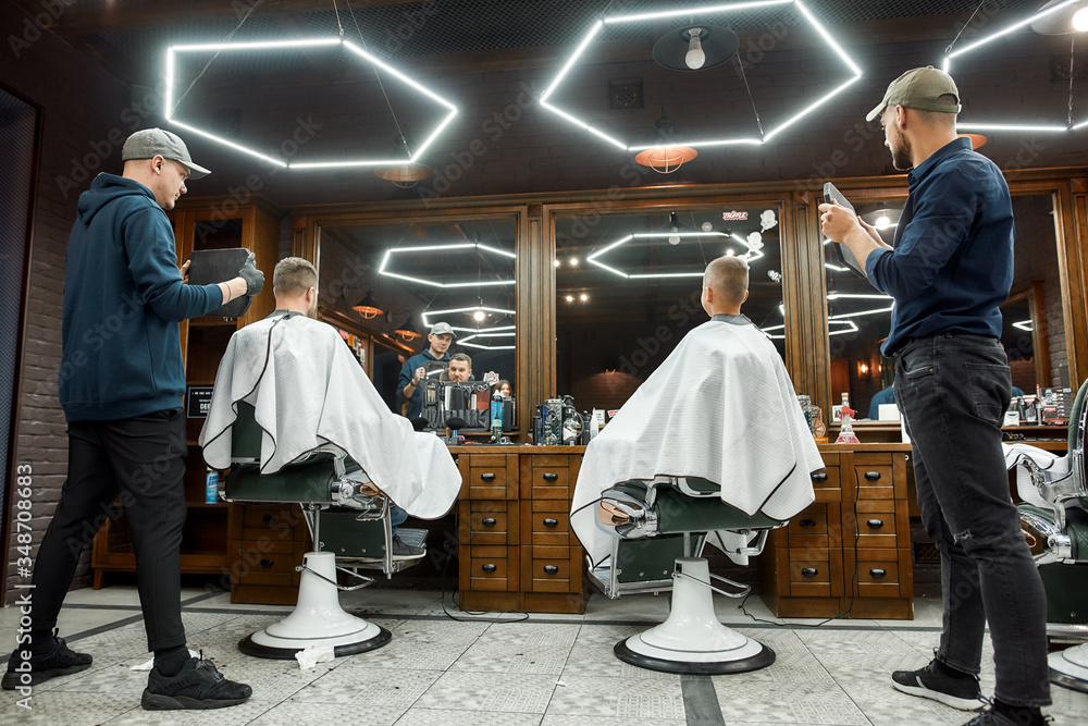 Foto de Two barbers holding mirrors and showing haircuts to father and ...