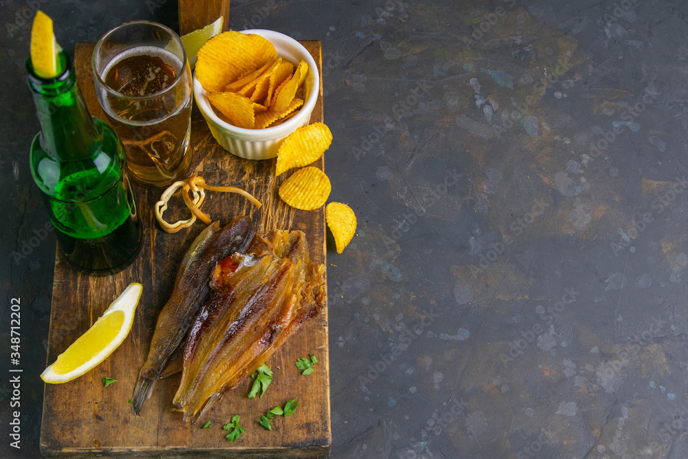 Dried blue whiting fish with beer, lemon and potato chips on dark ...