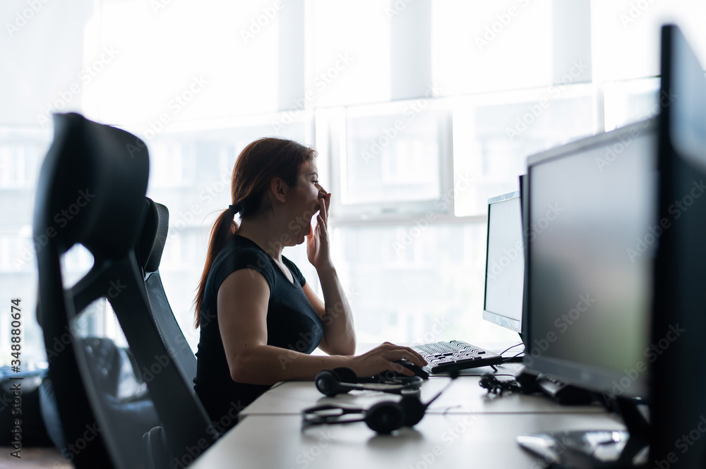 Tired woman in a black T-shirt works in an empty office and yawns at ...