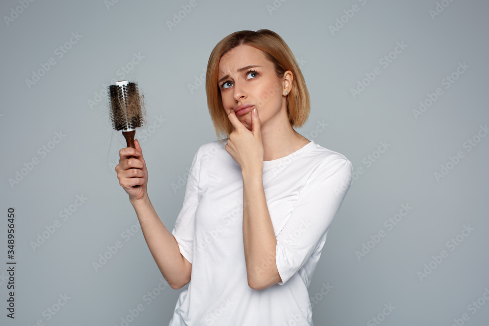 Blonde young worried woman holding hairbrush with unexpected hair loss ...