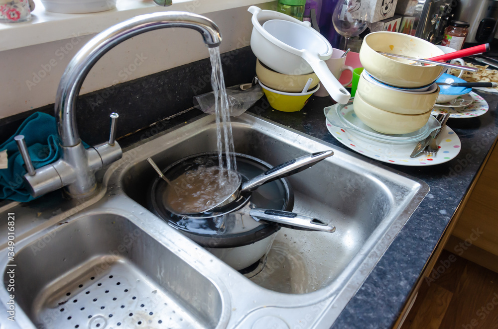 Running water from a tap fills saucepans soaking in a kitchen sink ...