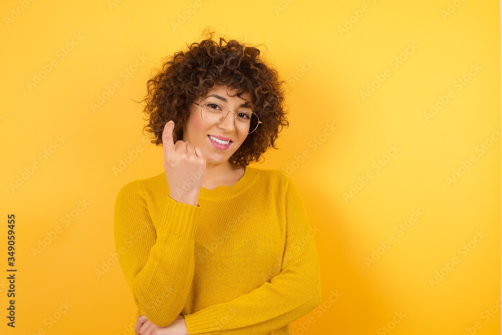 Young Arab woman with curly hair wearing yellow sweater standing over ...