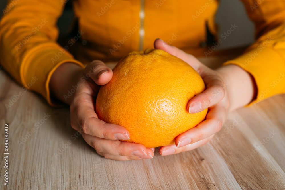 Whole grapefruit in hands of a person indoors at home. The colors of ...