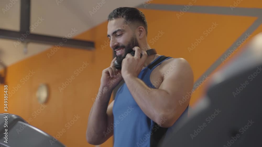 Happy Middle Eastern man adjusting treadmill in gym, putting on ...