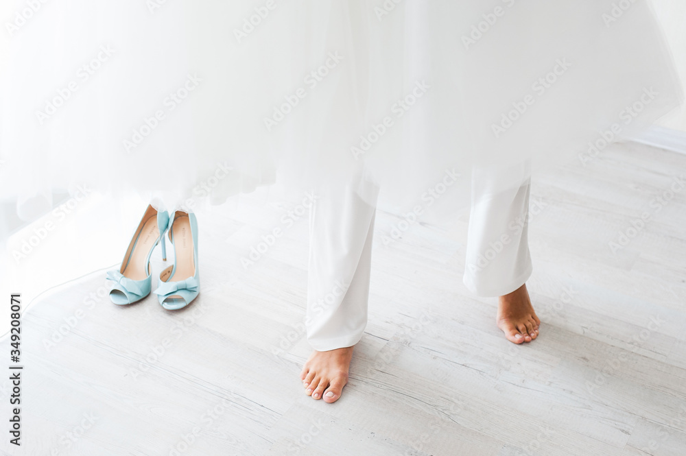 Barefoot bride in white trousers stands next to blue wedding shoes ...