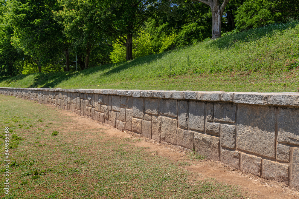 Long low rusticated stone block retaining wall in an outdoor park ...