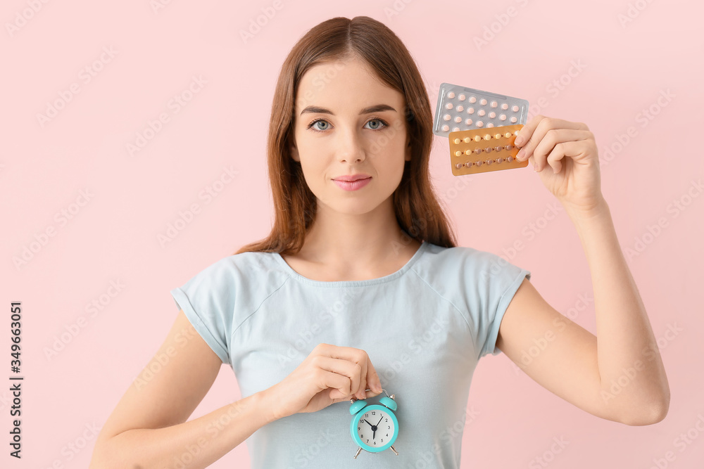 Young woman with birth control pills and clock on color background ...