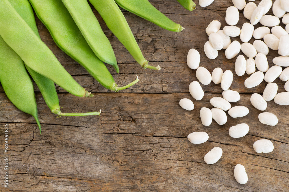Uncooked dried white haricot beans with fresh raw green beans pod plant on rustic table. Heap of ...