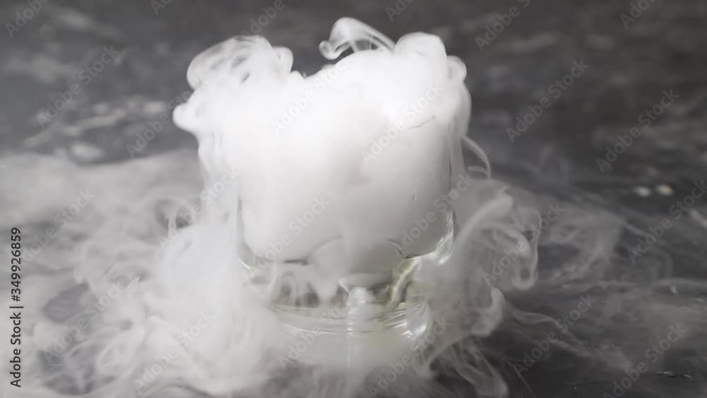 Dry ice fog flow from the transparent drinking glass on black concrete ...