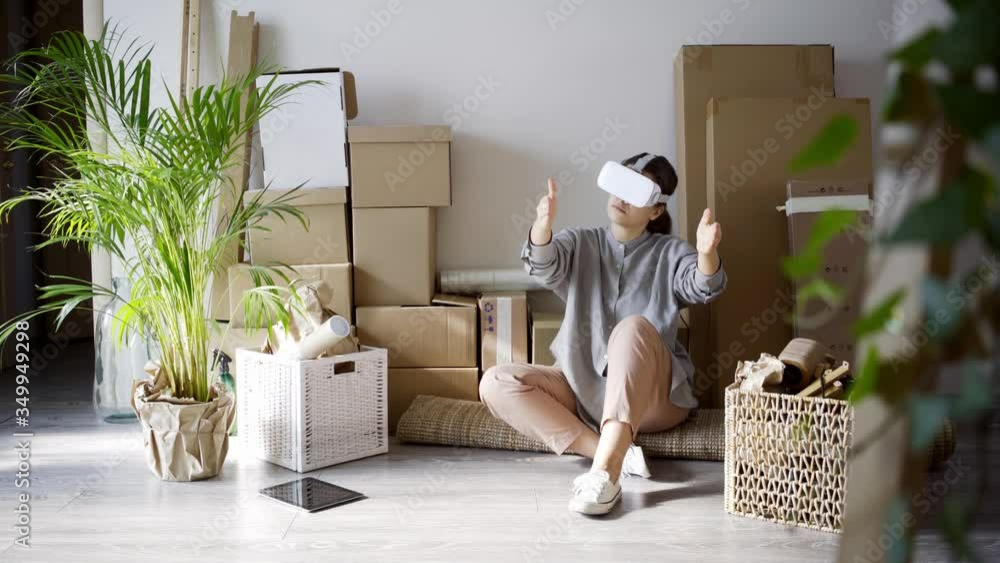 Young woman sitting on floor among cardboard boxes in VR headset while ...