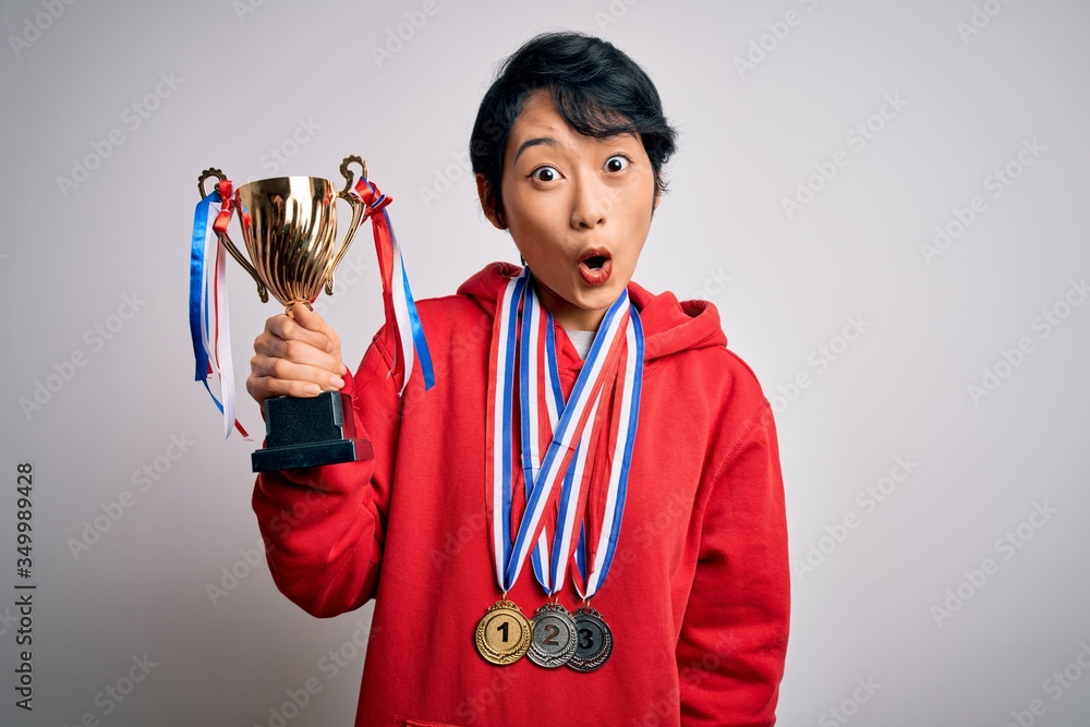 Young beautiful asian girl winner holding trophy wearing medals over ...