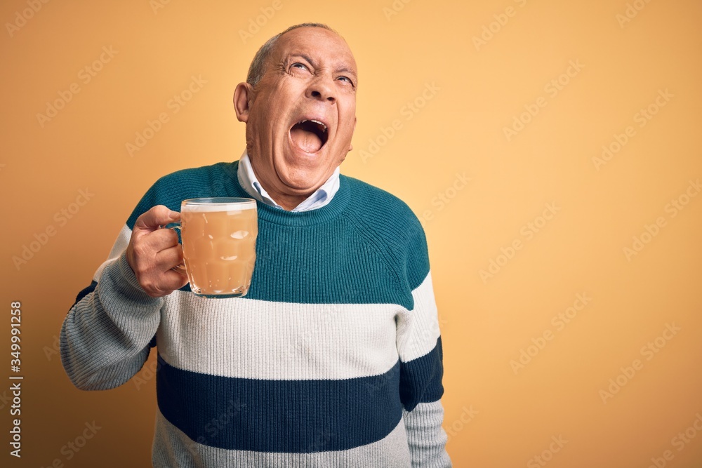 Senior handsome man drinking jar of beer standing over isolated yellow ...