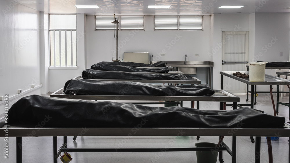 Covered human corpses on tables in a morgue / mortuary waiting for ...