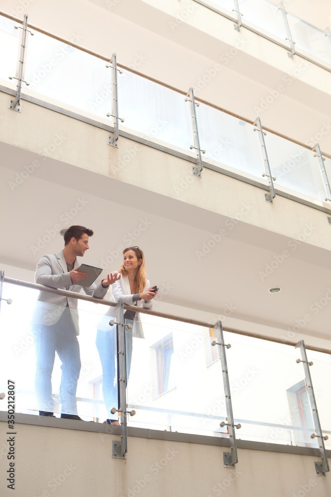 Young businesspeople talking in balcony of multi-storey building ...