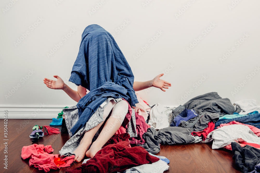 Kid playing with face covered. Cute Caucasian girl sorting clothes ...
