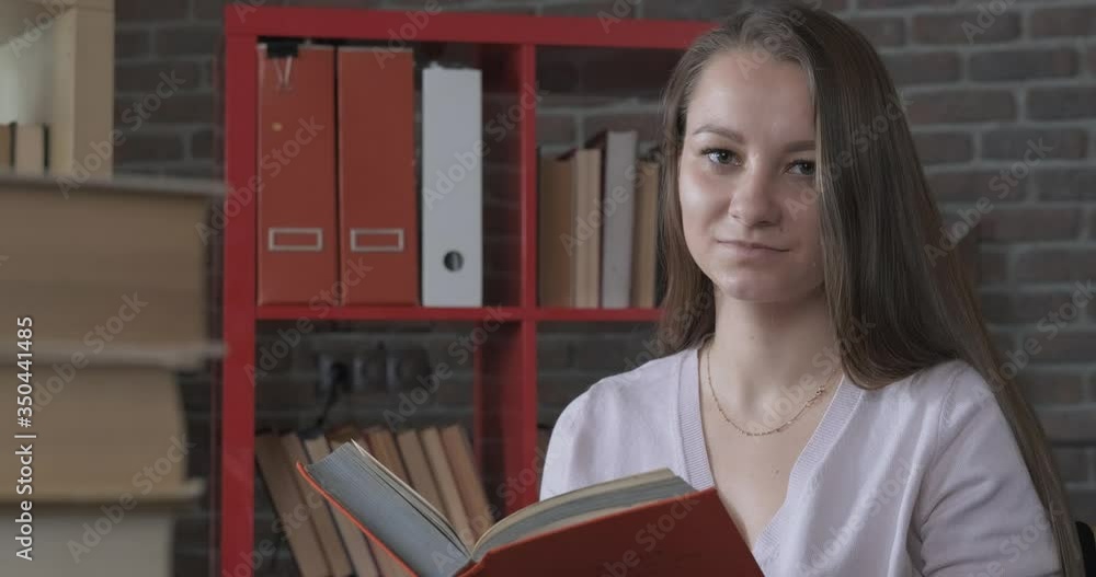 Beautiful and smart girl holds book with red cover in her hands, looks ...
