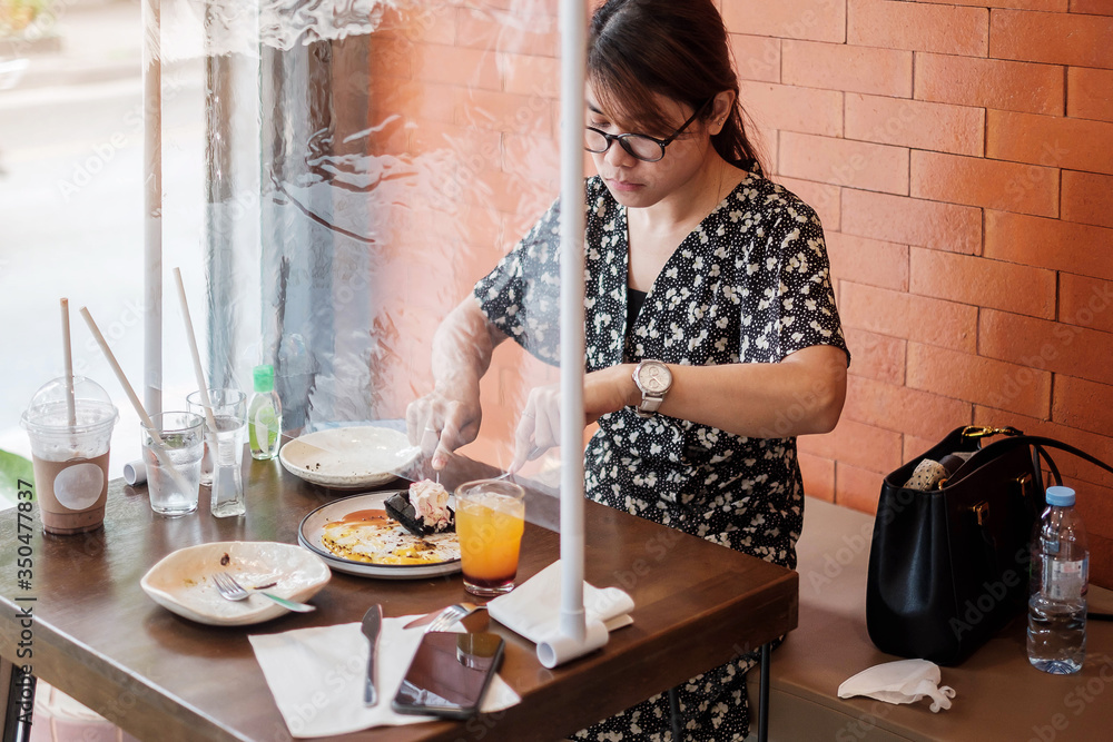 Asian woman eating food in restaurant with separated of shield plastic ...