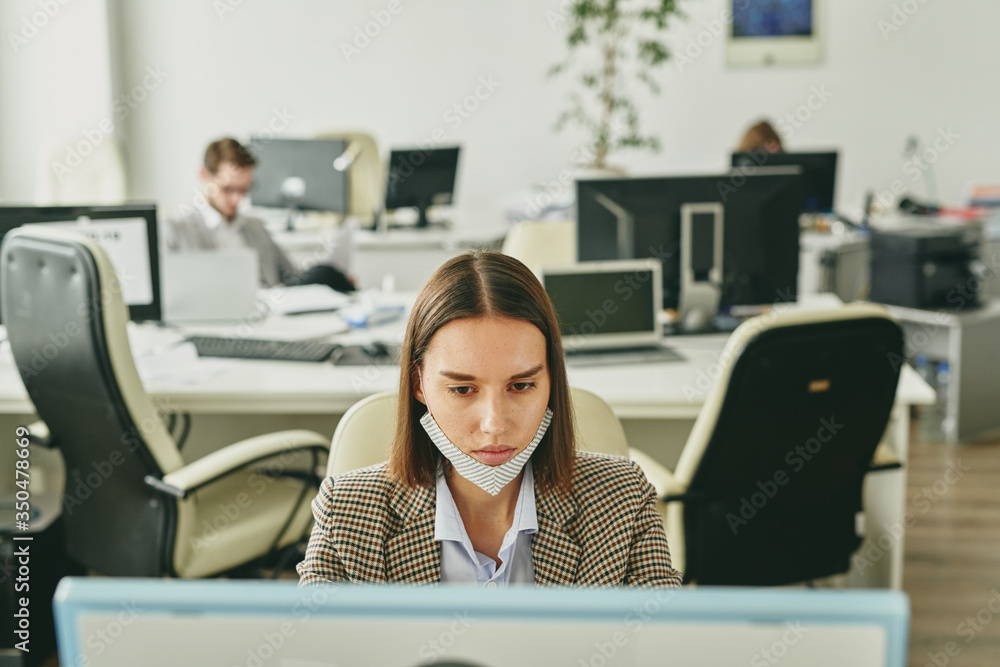 Attractive young woman with mask on chin using modern computer while ...