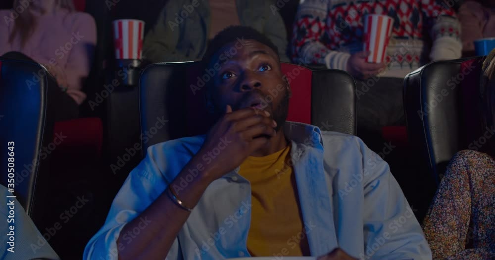 Close up of handsome guy watching action film in cinema. Young african ...