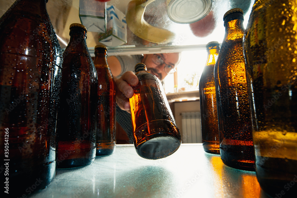 Caucasian man takes cold refreshing beer from out the fridge, inside ...