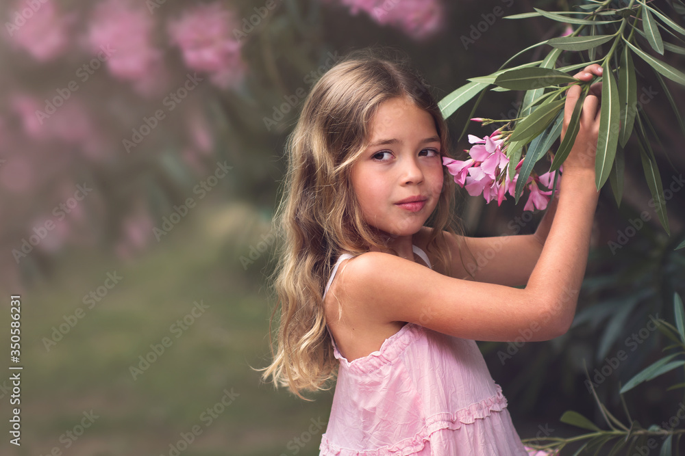 Young girl is smelling oleander in the park, girl looking at camera ...