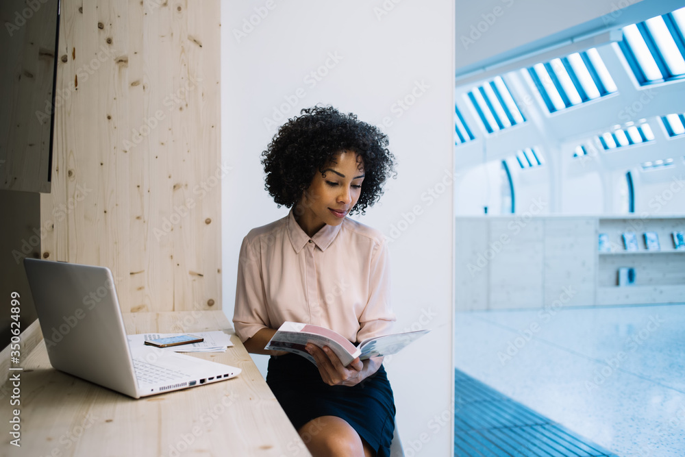 Successful young black female employee looking through catalog in ...
