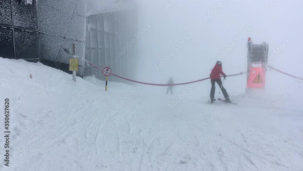 Dangerous mountain skiing, hard snowstorm. Woman skier crosses the red ...