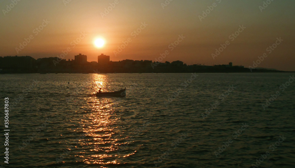 Puesta de sol sobre un pueblo de costa, el sol se refleja en el mar, en ...