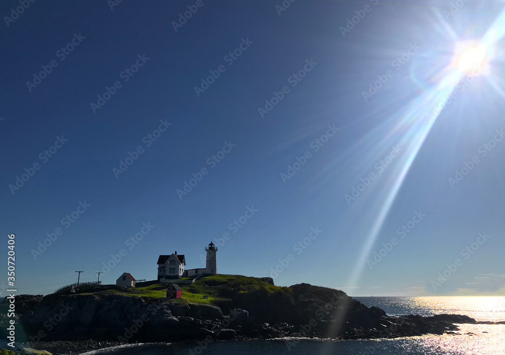 Silhouette and lens flare over a distant lighthouse near the ocean's ...