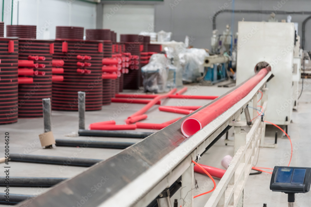 Factory for the production of plastic pipes.conveyor. The red pipe runs ...