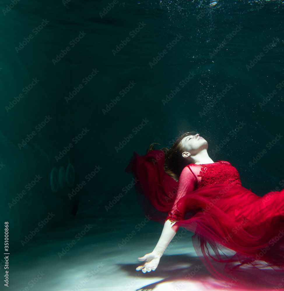 Beautiful girl underwater in a red dress swims in the pool. Tenderness ...