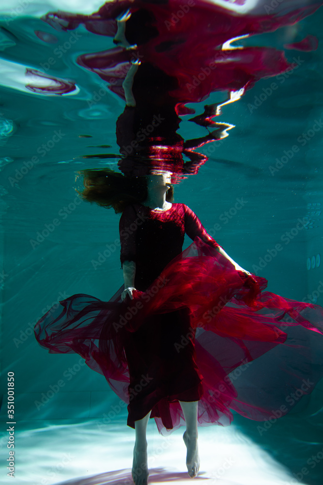 Beautiful girl underwater in a red dress swims in the pool. Tenderness ...