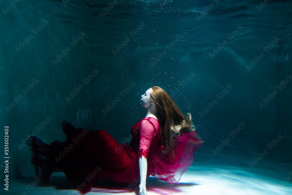 Beautiful girl underwater in a red dress swims in the pool. Tenderness ...