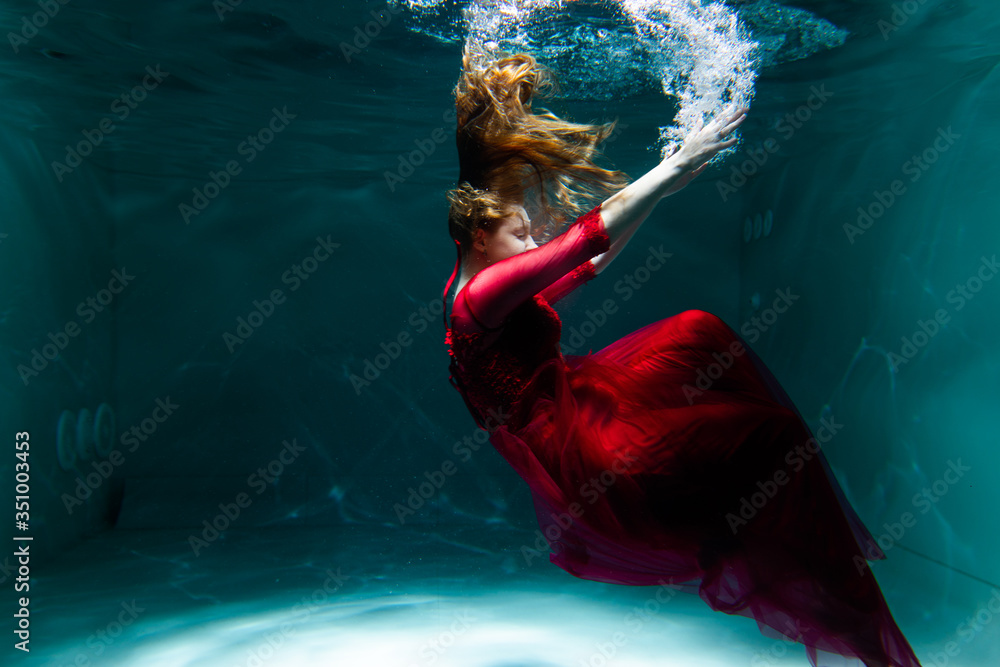 Beautiful girl underwater in a red dress swims in the pool. Tenderness ...