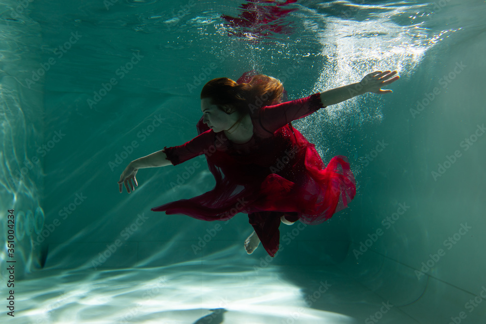 Beautiful girl underwater in a red dress swims in the pool. Tenderness ...