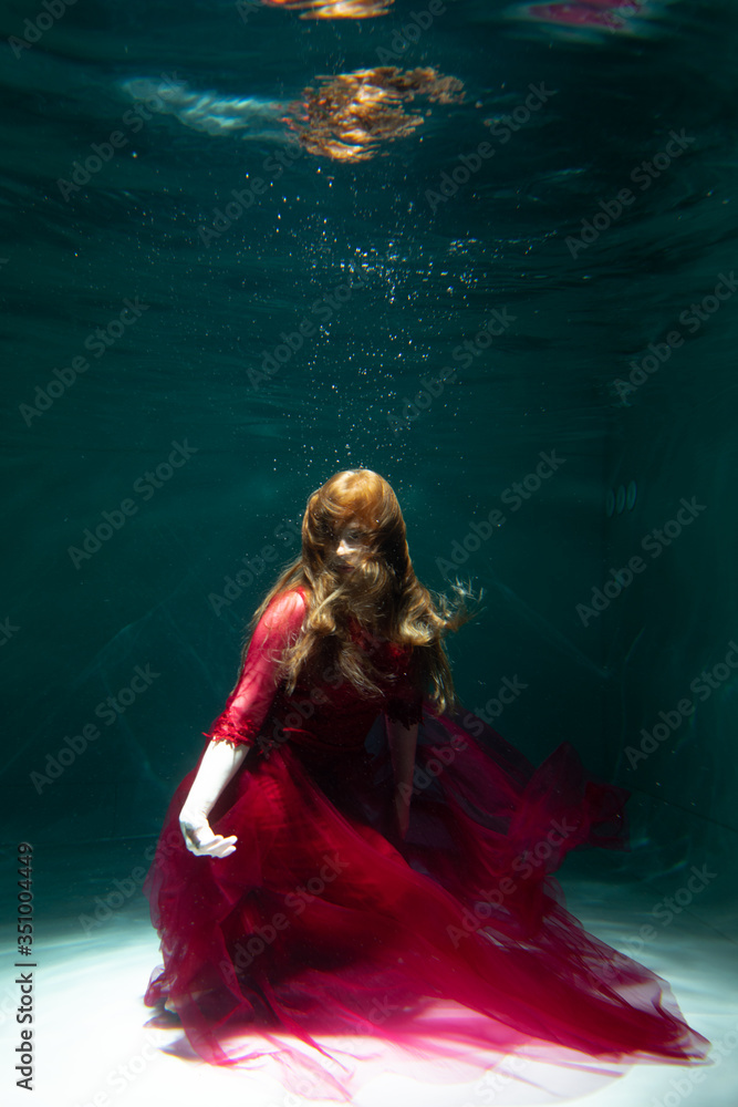 Beautiful girl underwater in a red dress swims in the pool. Tenderness ...