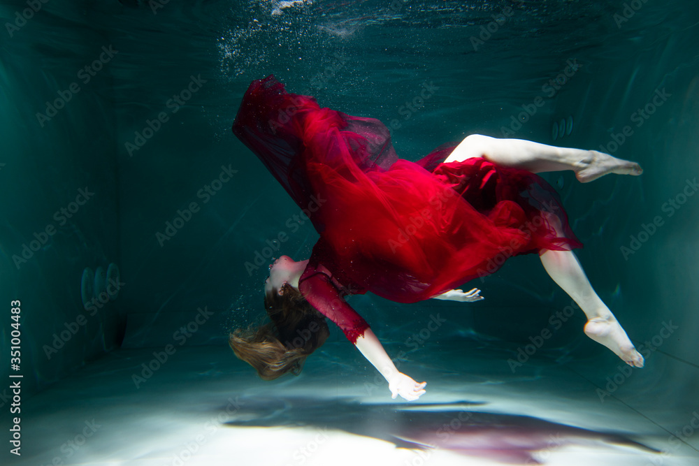 Beautiful girl underwater in a red dress swims in the pool. Tenderness ...