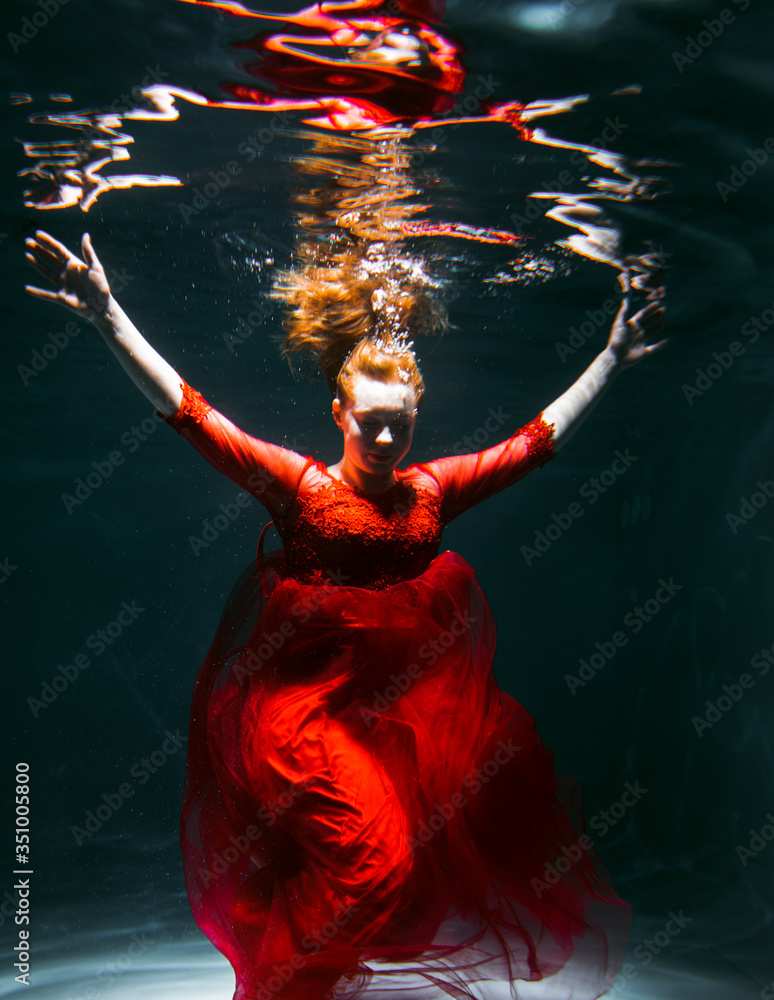 Beautiful girl underwater in a red dress swims in the pool. Tenderness ...
