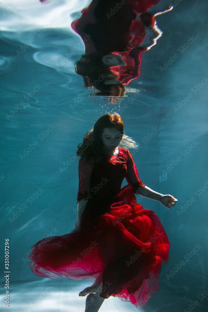 Beautiful girl underwater in a red dress swims in the pool. Tenderness ...