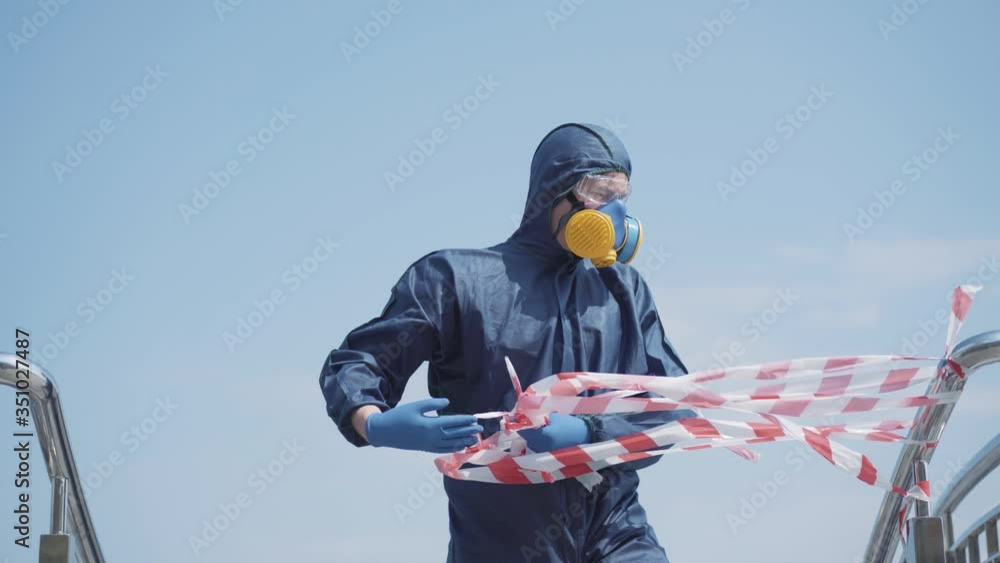Man in chemical suit tearing off caution tape and leaving. Portrait of ...