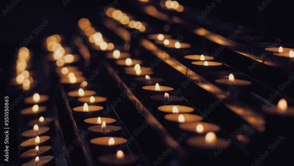 Rows of hundreds burning votive candles in dark moody sacral ...