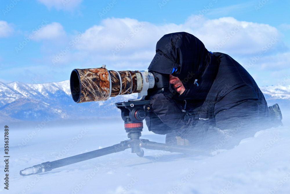 Winter photography, man in the snow with camera. Snow lake with ice in ...